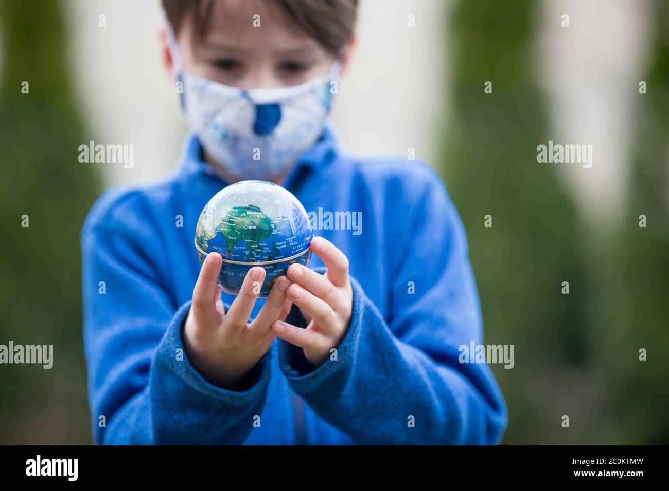 School child, holding small globe, looking sad at the world during ...