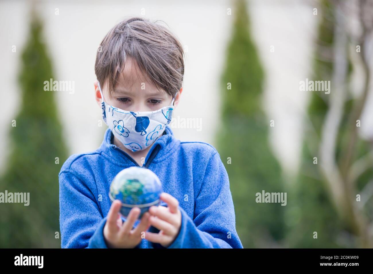 School child, holding small globe, looking sad at the world during ...