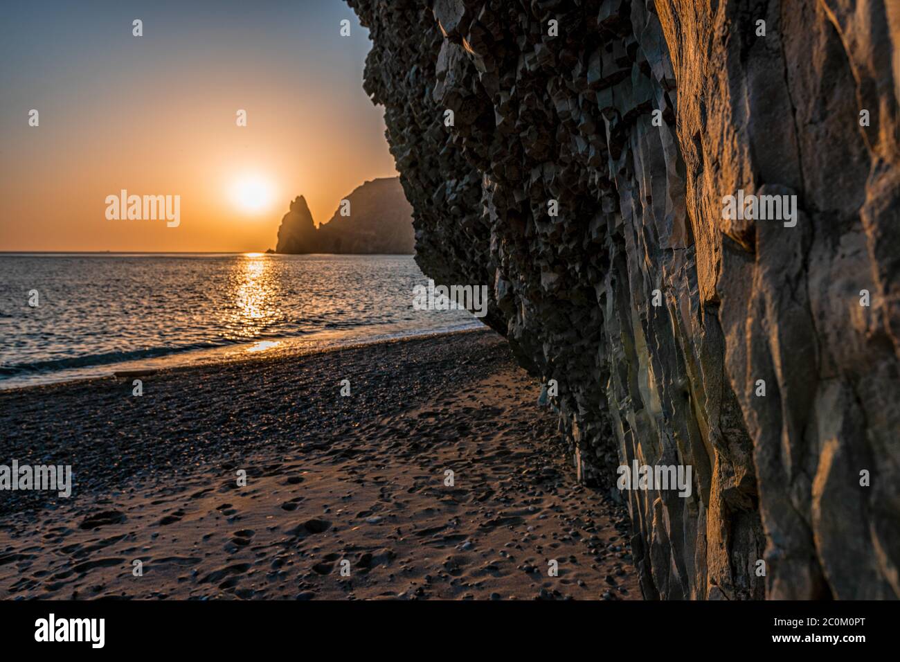 view of the sunset sea and the beach, the rock volcanic rock is lit by ...