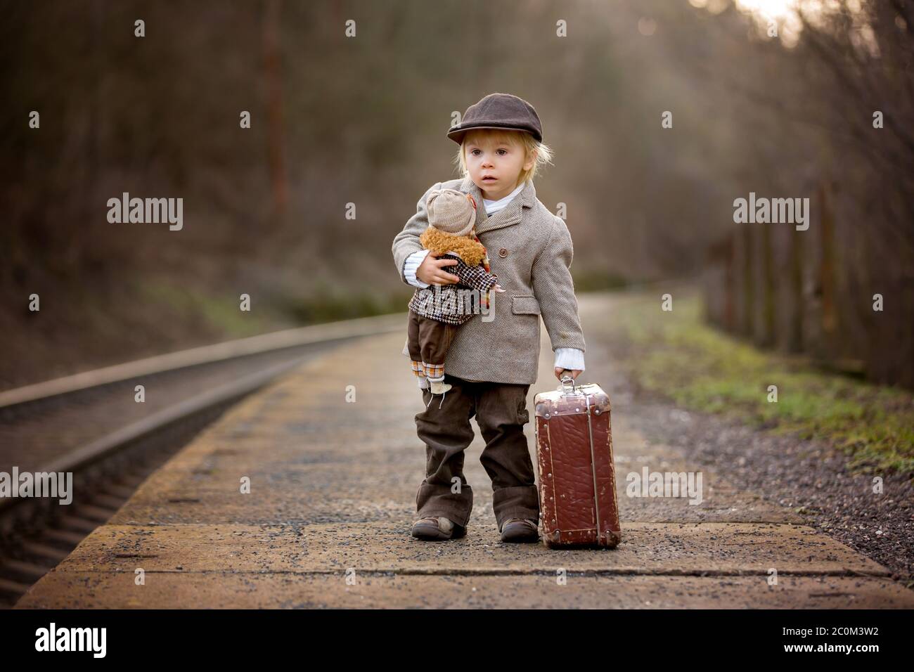 Adorable boy on a railway station, waiting for the train with suitcase ...