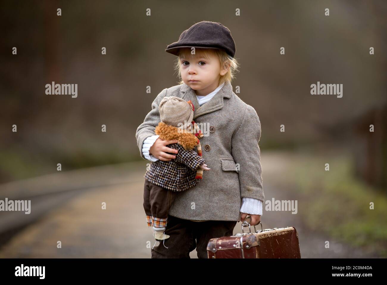 Adorable boy on a railway station, waiting for the train with suitcase ...