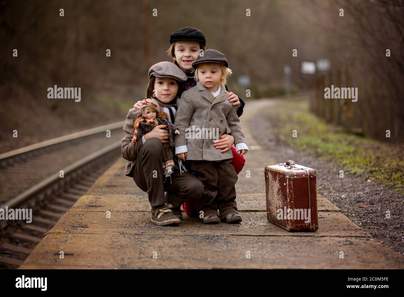 Adorable boys on a railway station, waiting for the train with suitcase ...