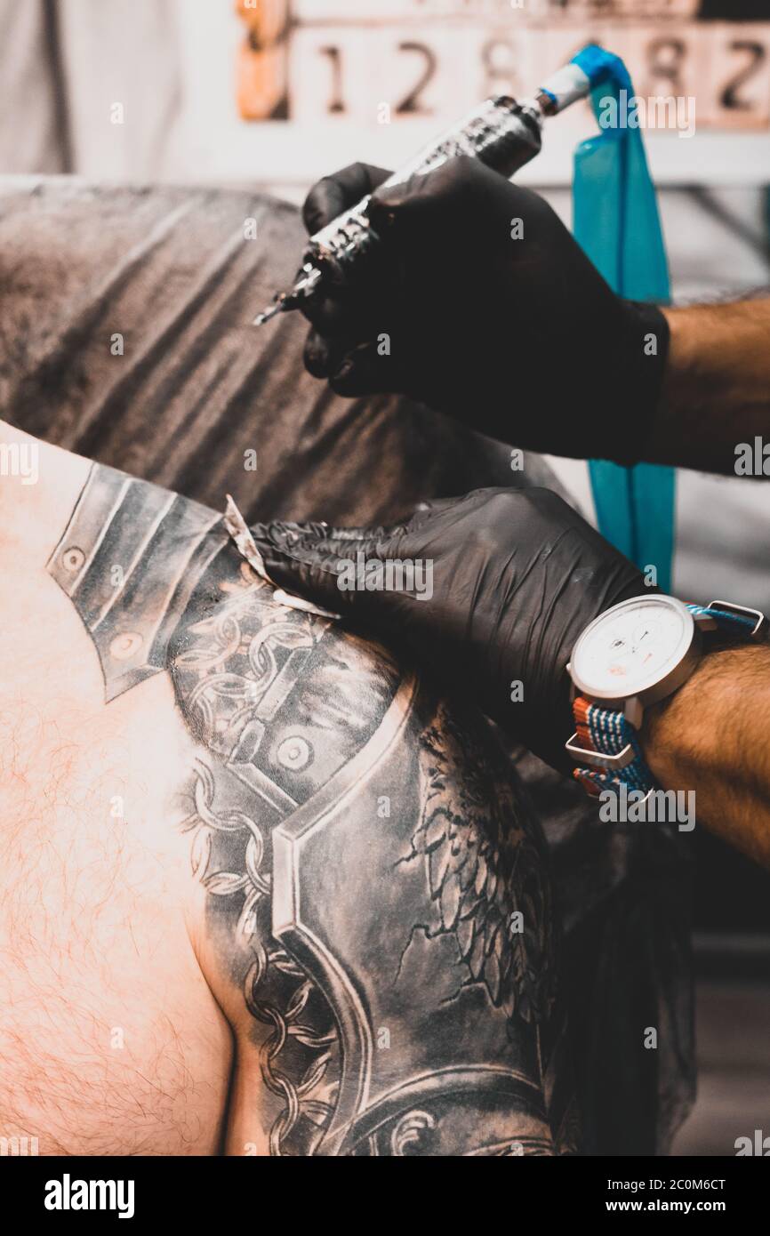 Tattoo salon. The tattoo master is tattooing a man on his shoulder ...