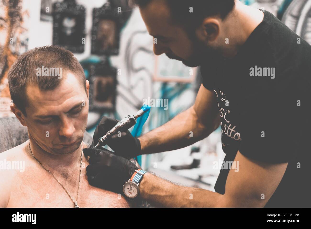 Tattoo salon. The tattoo master is tattooing a man on his shoulder ...