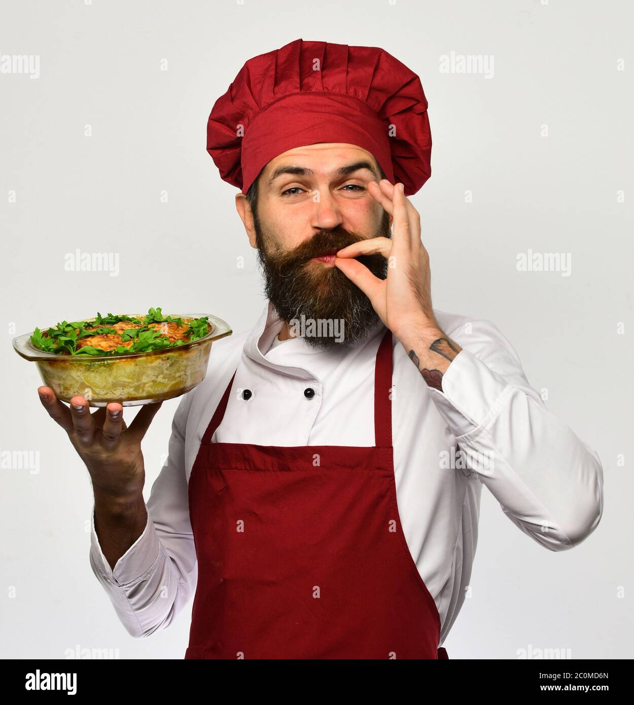 Cook with happy face in burgundy uniform holds baked dish. Man with ...
