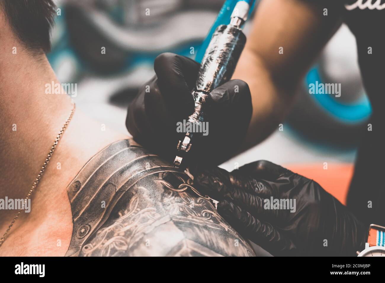 Tattoo salon. The tattoo master is tattooing a man on his shoulder ...