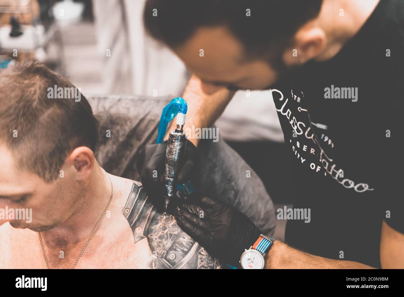 Tattoo salon. The tattoo master is tattooing a man on his shoulder ...