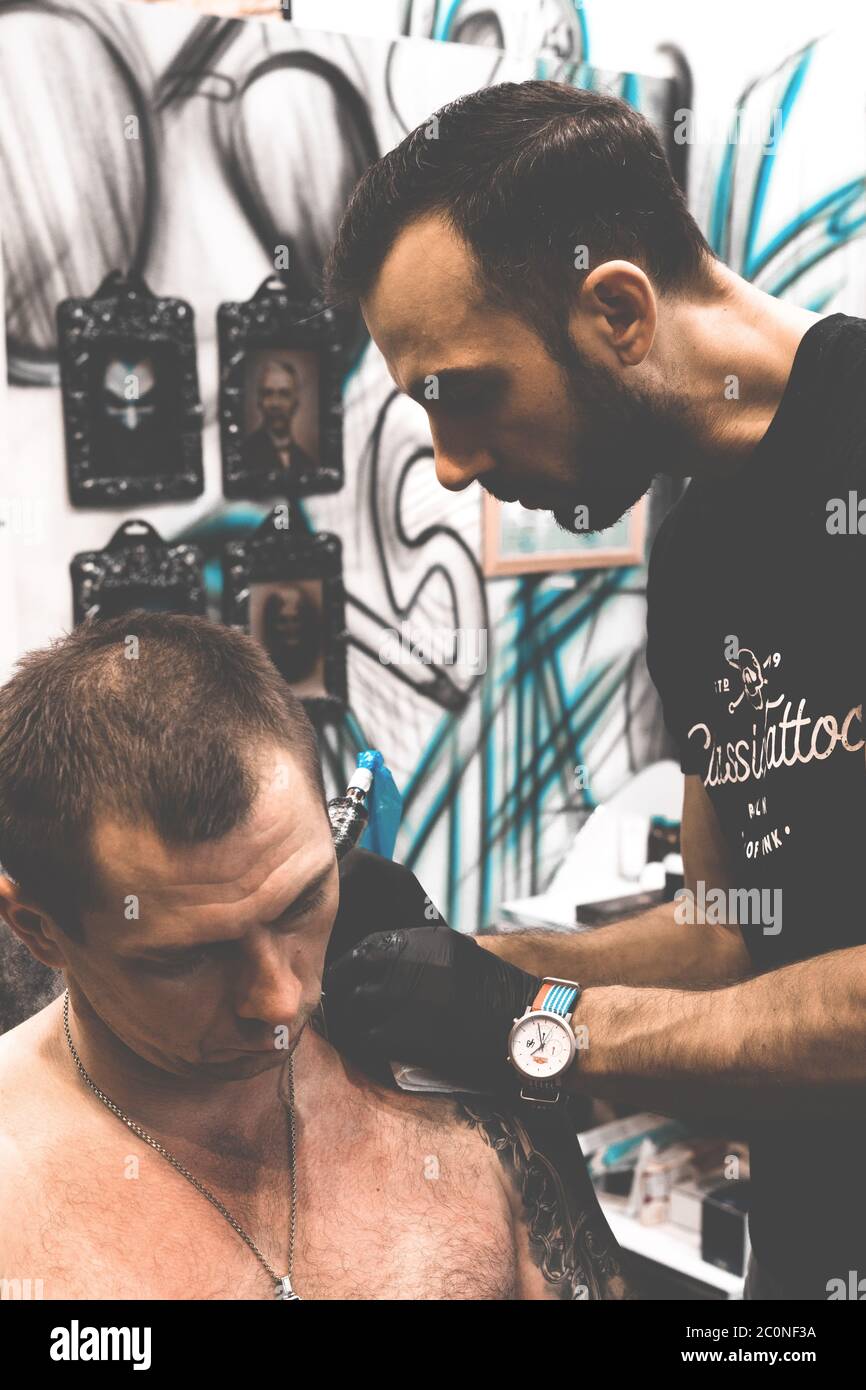 Tattoo salon. The tattoo master is tattooing a man on his shoulder ...