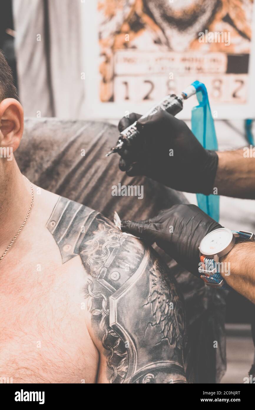 Tattoo salon. The tattoo master is tattooing a man on his shoulder ...