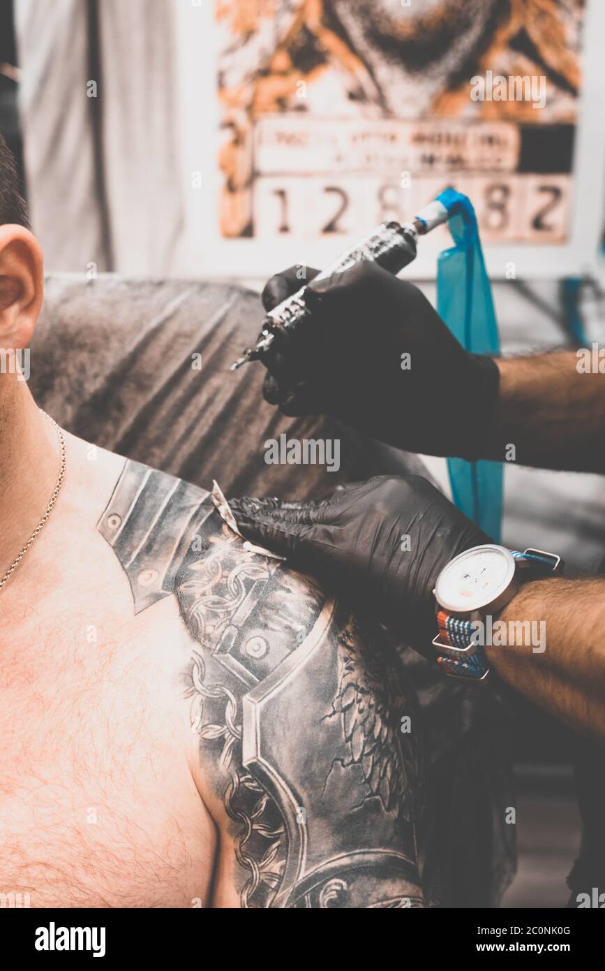 Tattoo salon. The tattoo master is tattooing a man on his shoulder ...