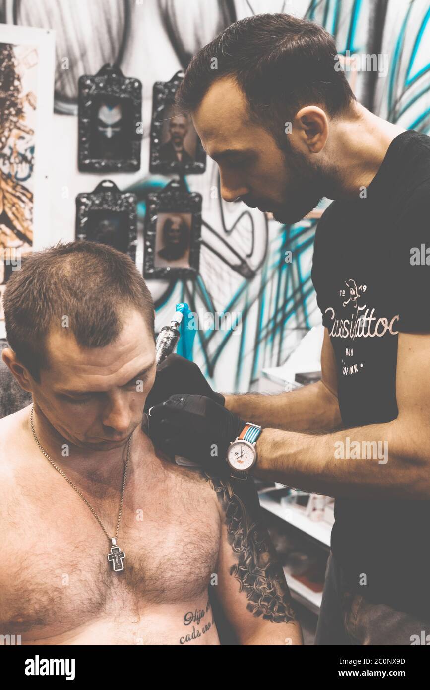 Tattoo salon. The tattoo master is tattooing a man on his shoulder ...