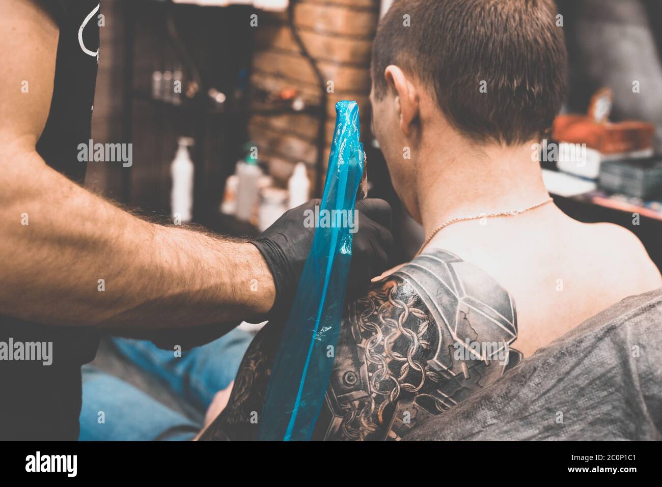 Tattoo salon. The tattoo master is tattooing a man on his shoulder ...