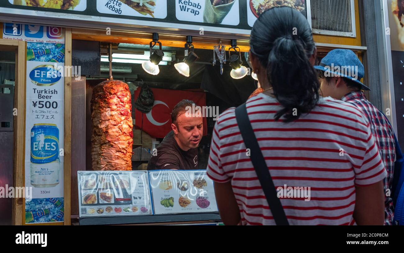 Customers lining up buying food from a kebab stall at Ameyayokocho ...