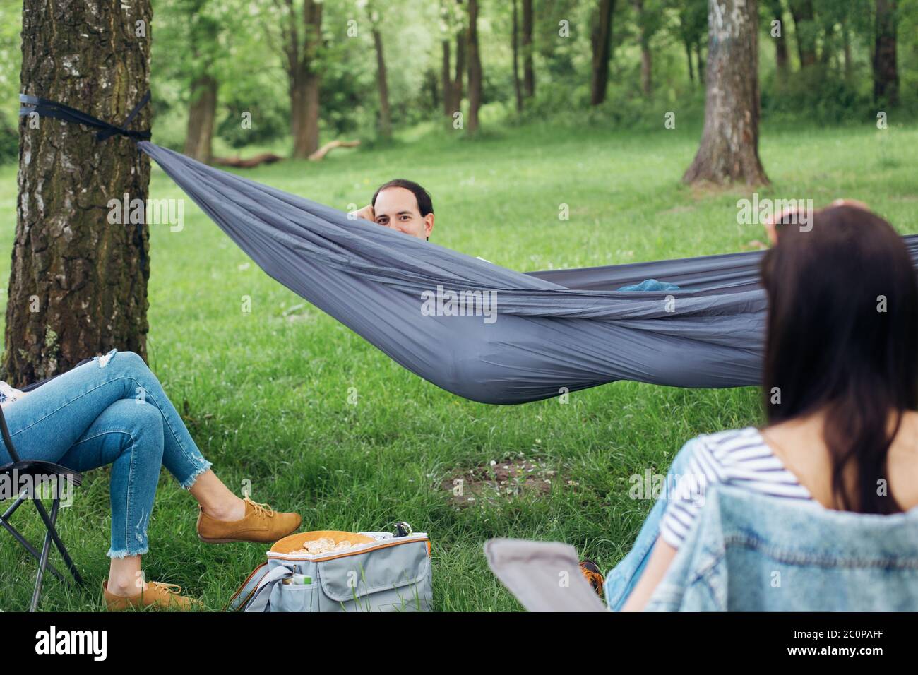 Friends chilling in hammock and on chairs among trees. Social ...