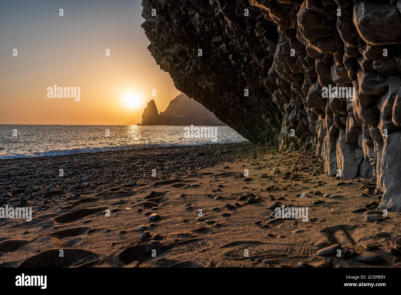 View of the sunset sea and the beach, the rock volcanic rock is lit by ...