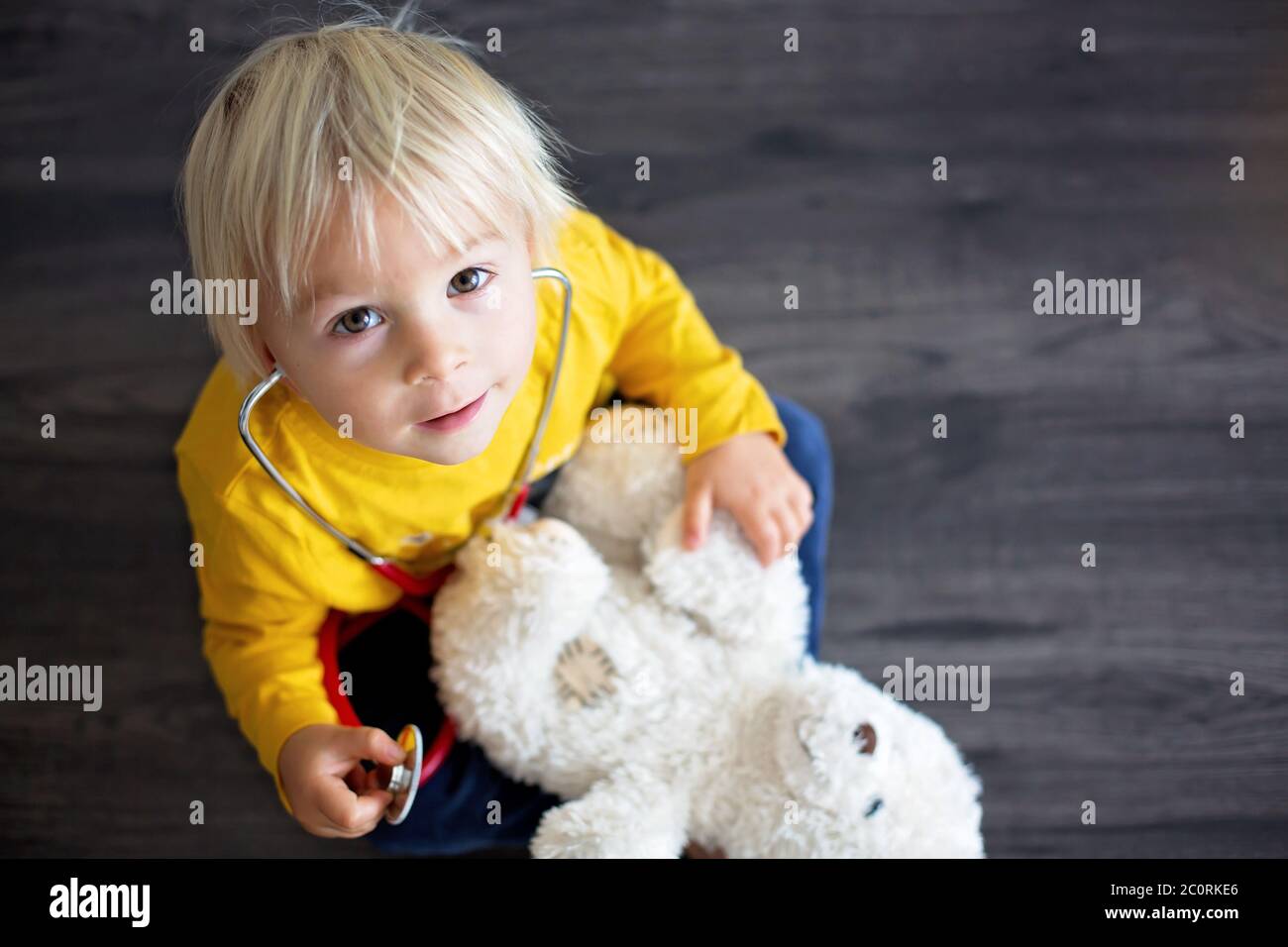 Sweet toddler child, playing doctor, examining teddy bear toy at home ...