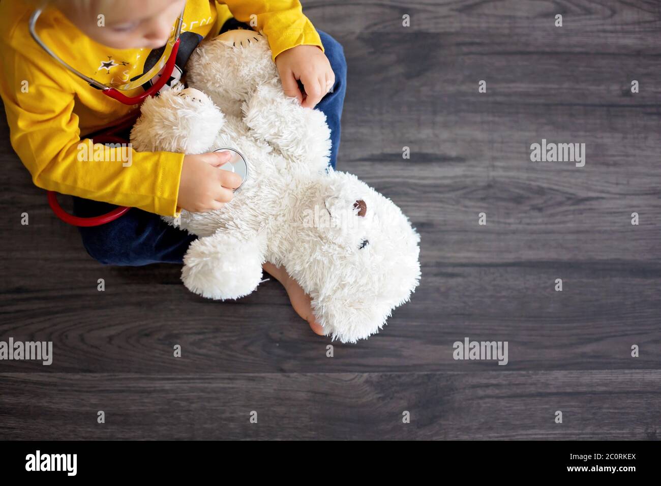 Sweet toddler child, playing doctor, examining teddy bear toy at home ...