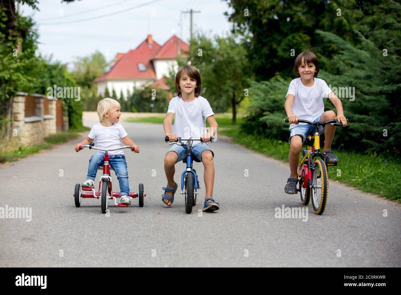 Three children, brothers, riding bike, tricycle and balance bike on the ...