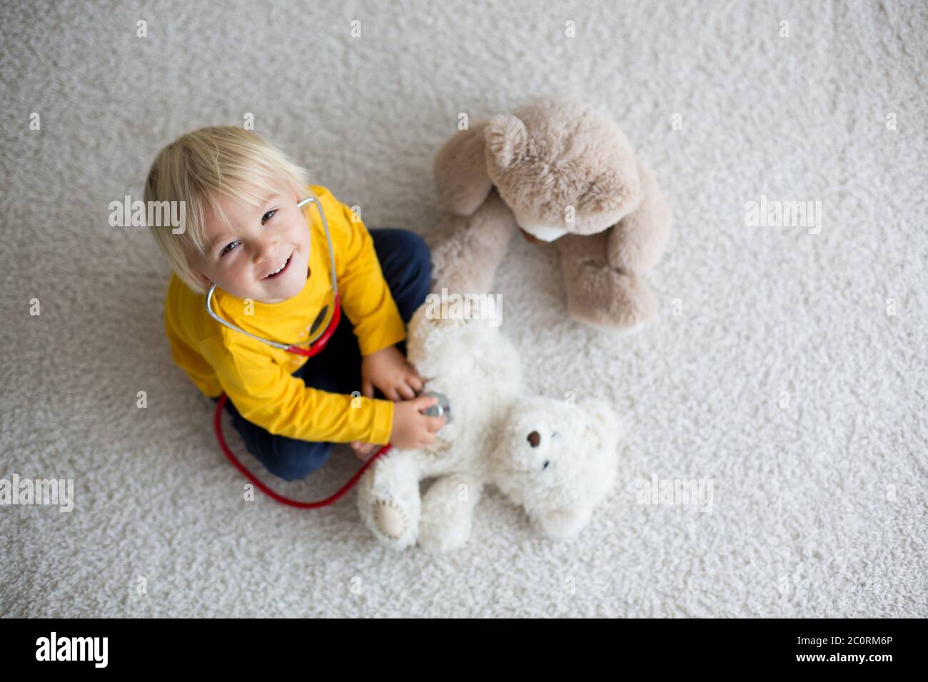 Sweet toddler child, playing doctor, examining teddy bear toy at home ...