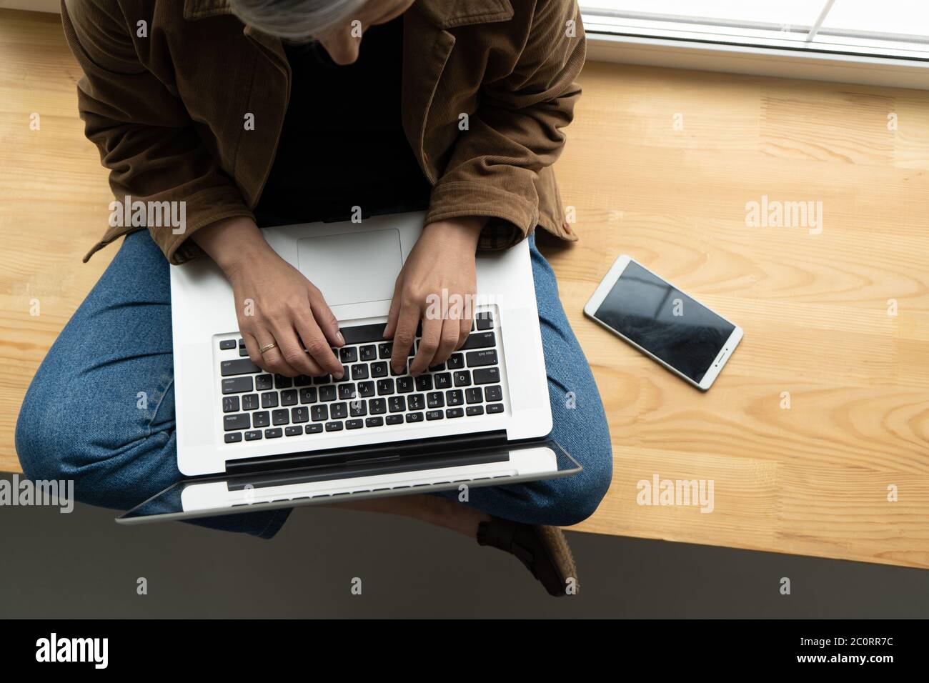 Grey haired businesswoman types at laptop keyboard sitting on wooden ...