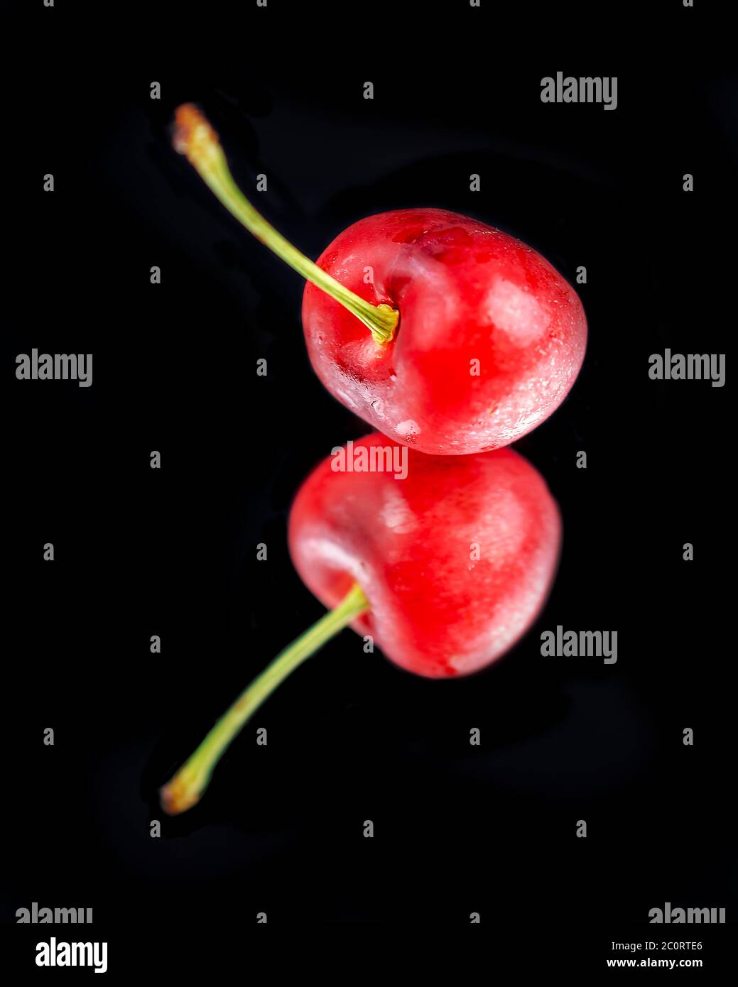 A single red cherry with stem on a mirror with reflection. Black ...