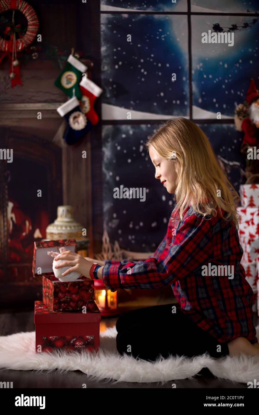 Cute preschool girl, sitting next to christmas tree, opening presents ...