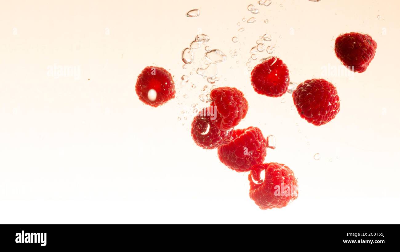 raspberry fruits making splash in water orange pastel background Stock ...