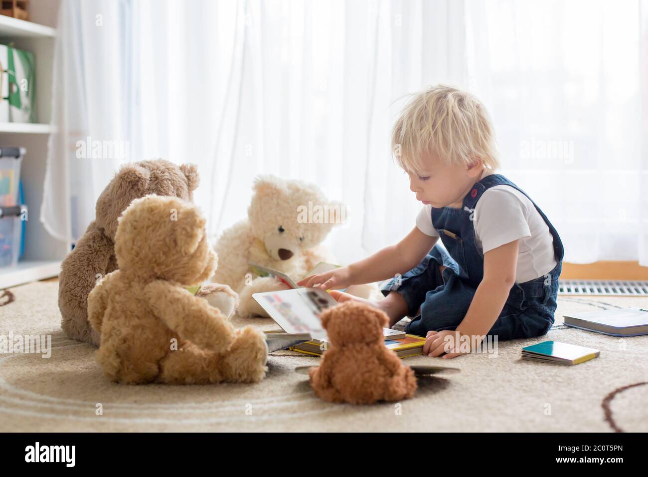 Little toddler boy, reading a book to his teddy bear friends at home ...