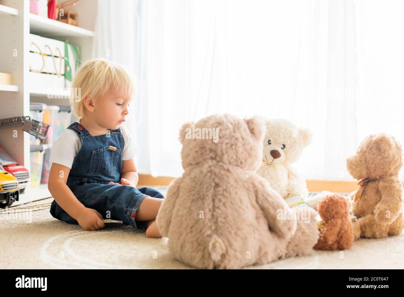 Little toddler boy, reading a book to his teddy bear friends at home ...