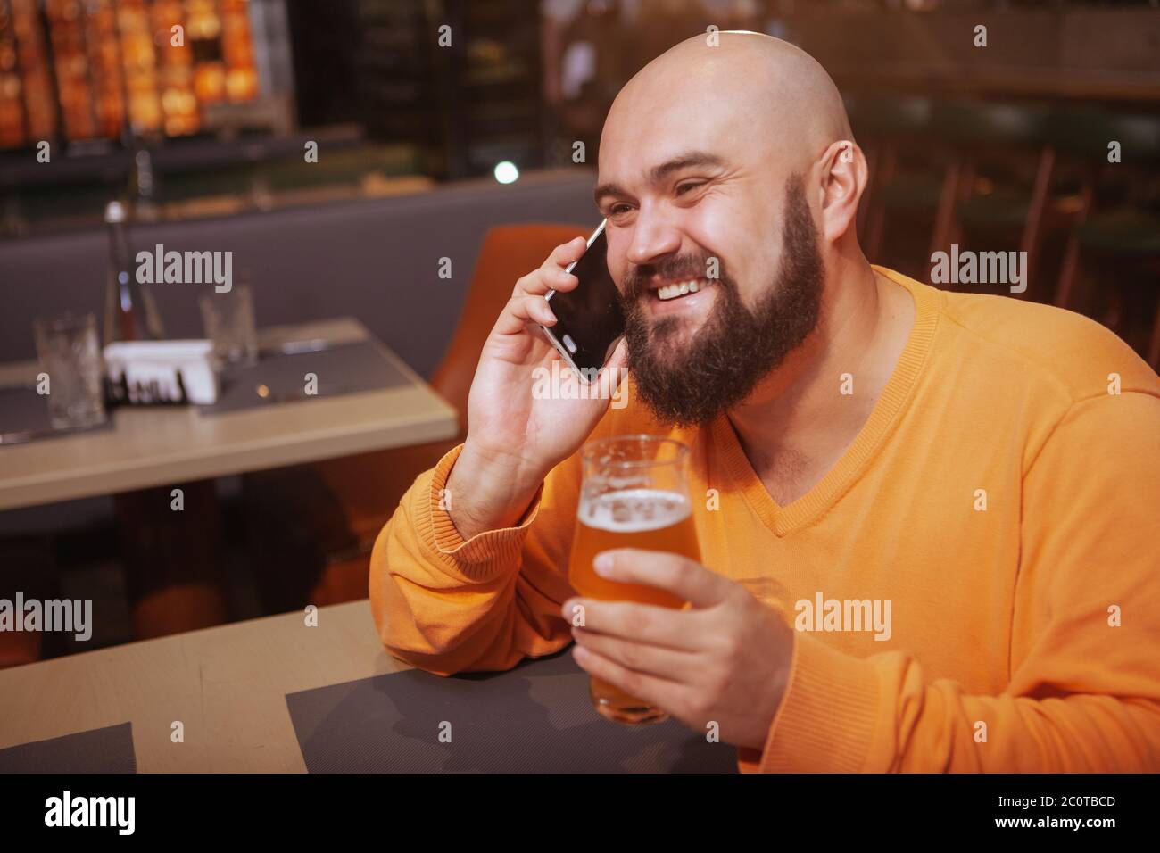 Happy man laughing, drinking beer and talking on the phone at the bar ...