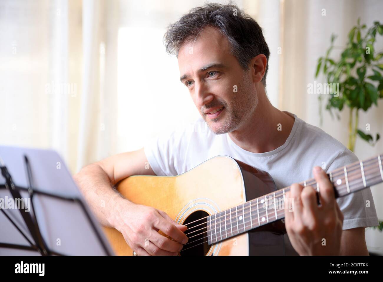 Detail of smiling man playing a song on a guitar looking at a score on ...