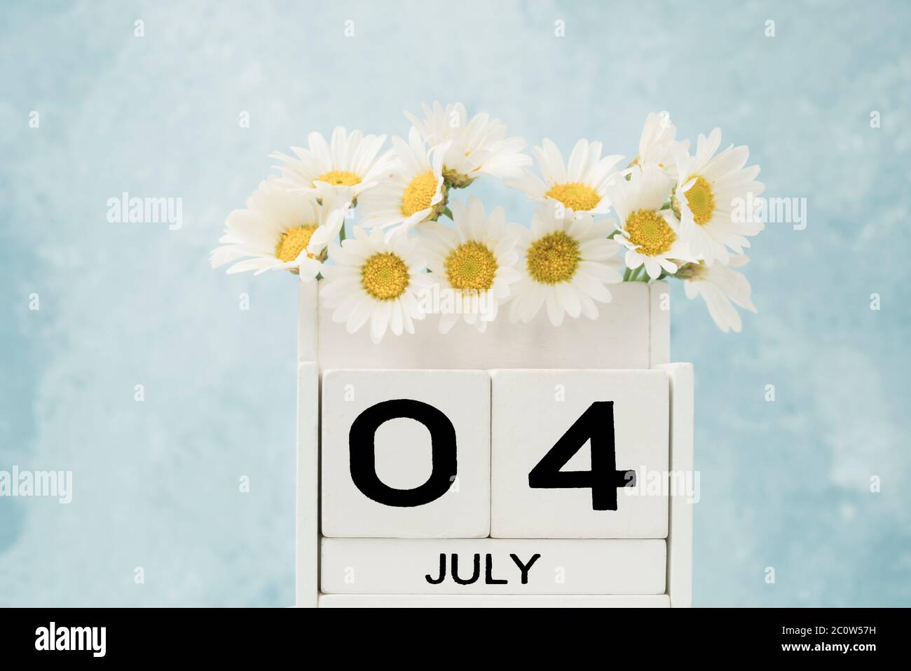 White cube calendar for july decorated with daisy flowers over blue ...