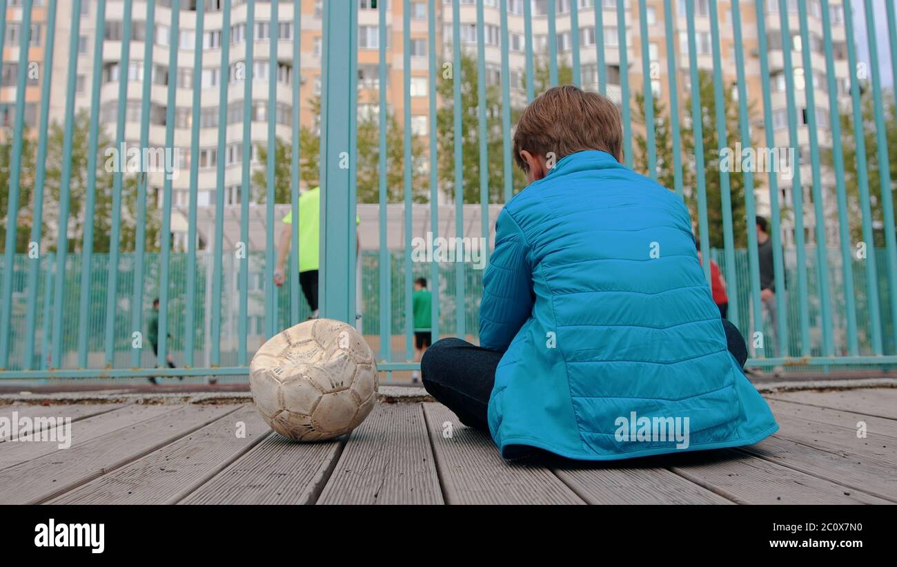 A little boy sitting on the bench near the deflated ball and watching ...