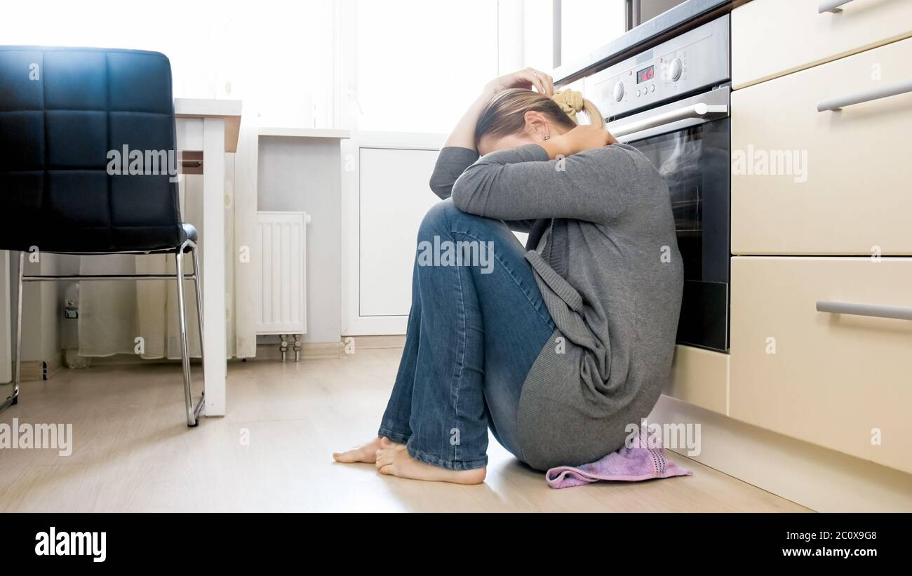 Youg woman crying on floor in kitchen. Problems in family relations and ...