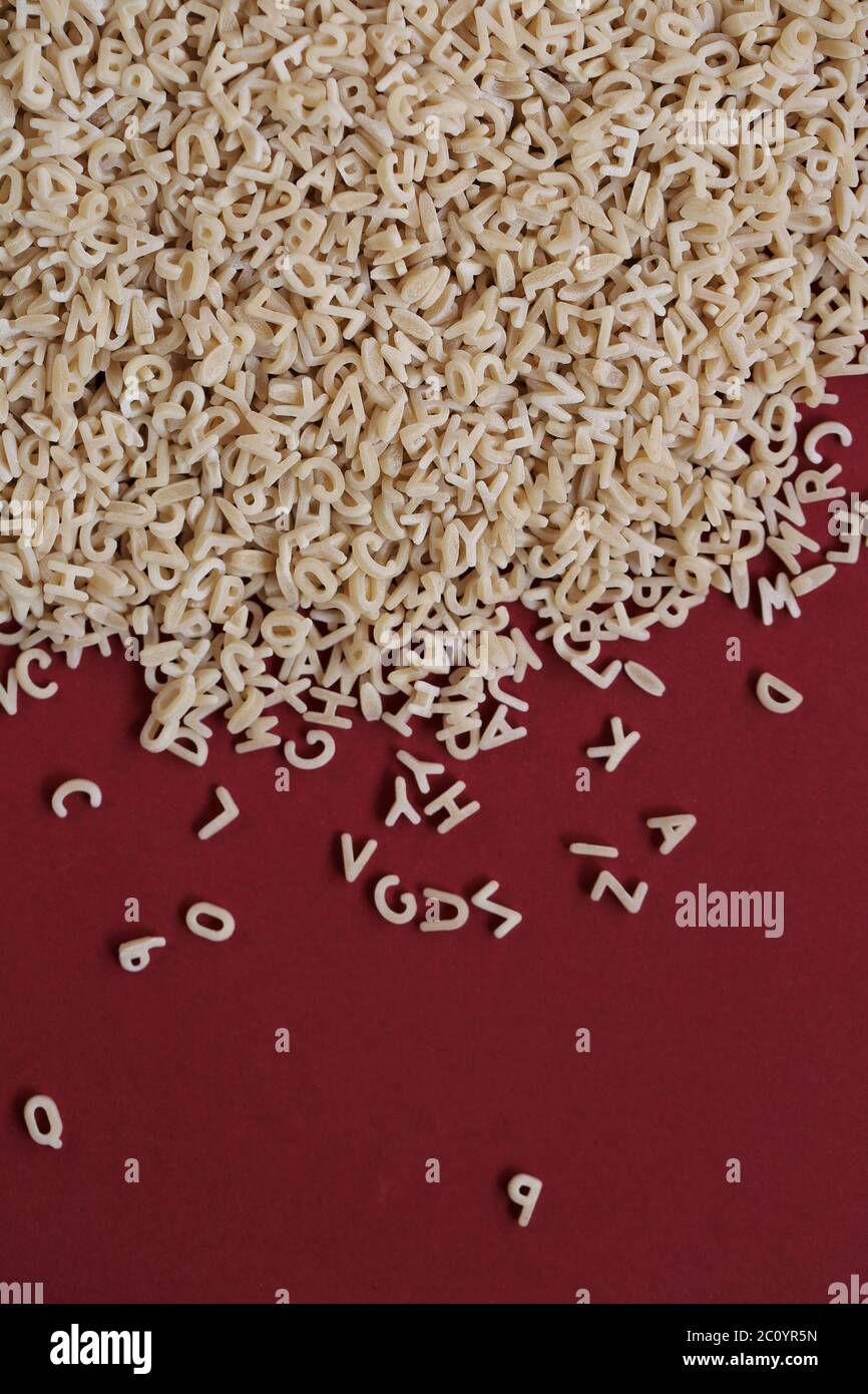 Pasta letters heap close-up on a bright burgundy background. uncooked ...