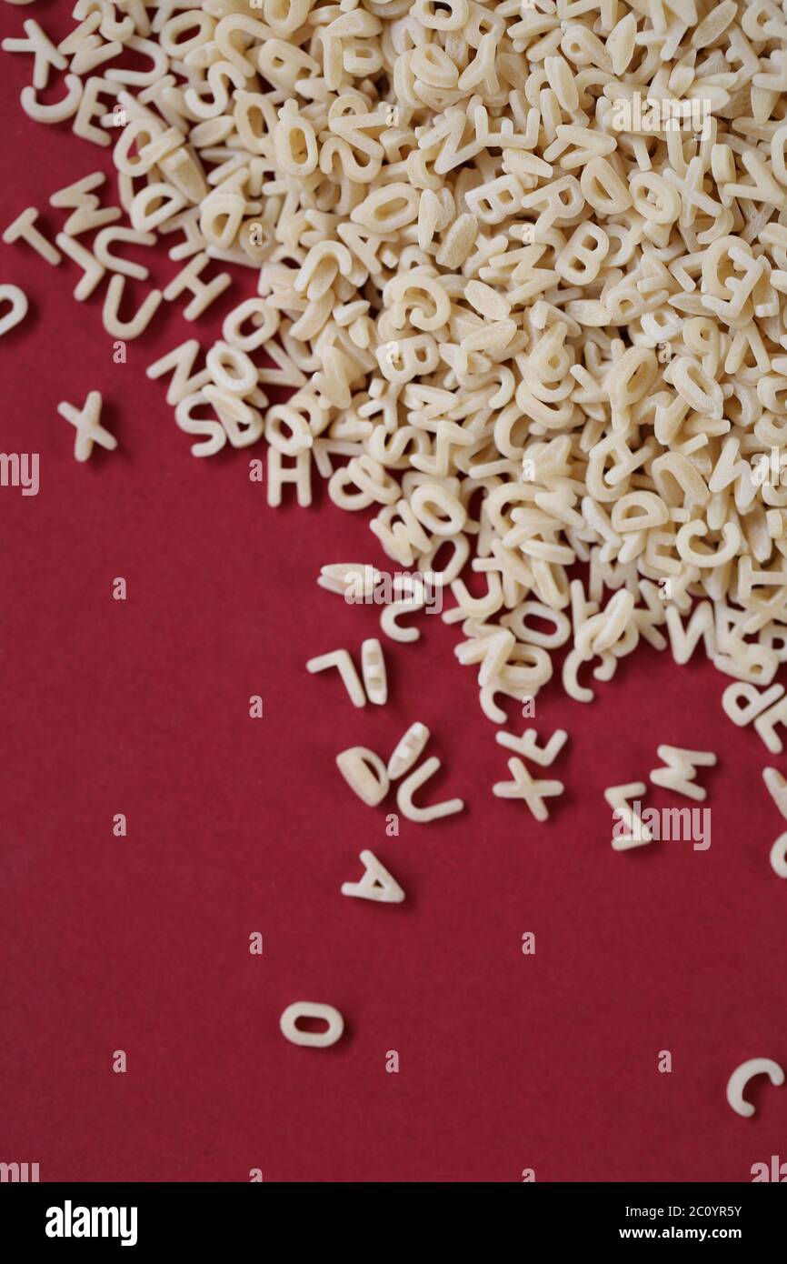 Pasta letters heap close-up on a bright burgundy background..Dry ...