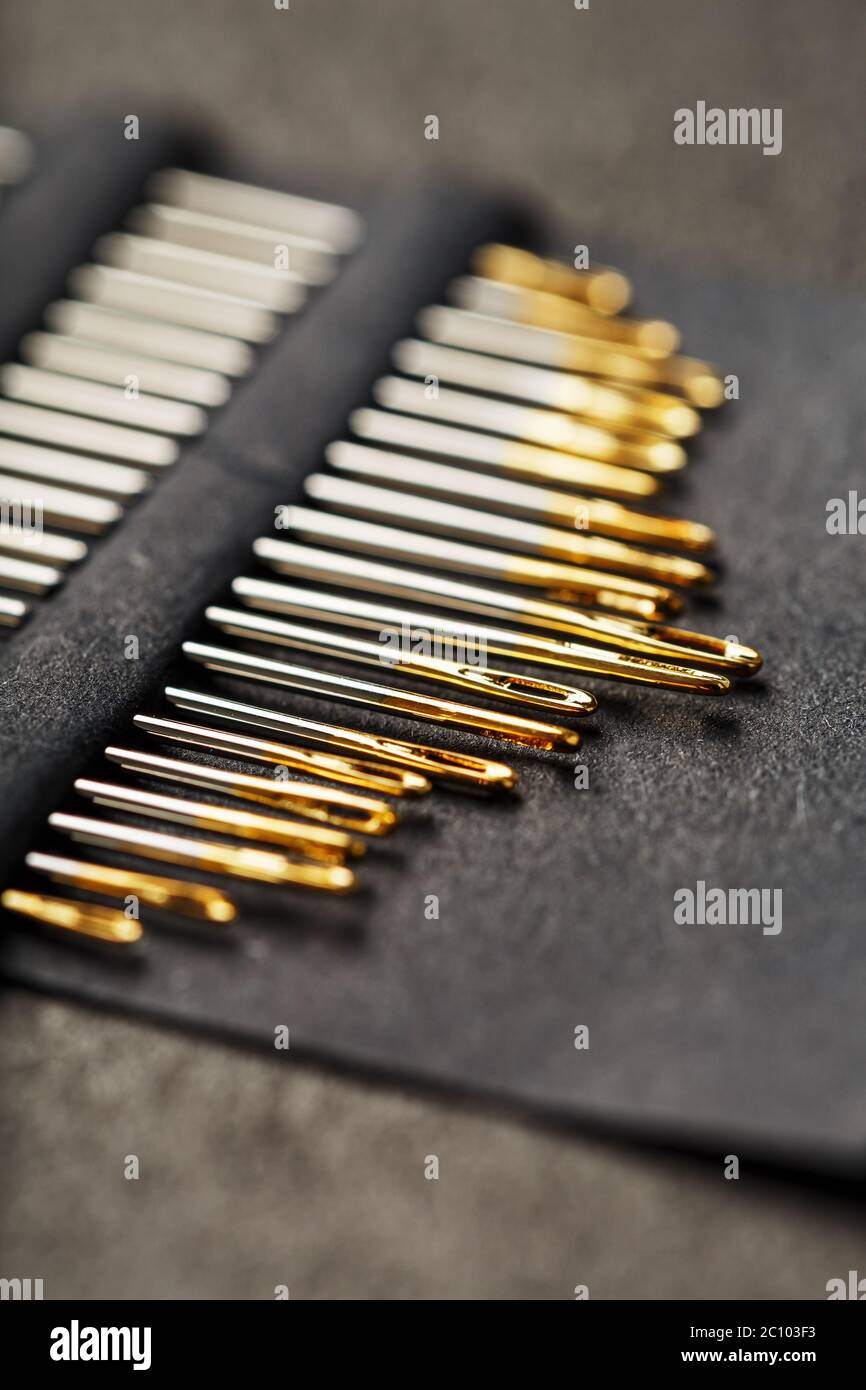 Gold sewing needles on a black background in a row Stock Photo - Alamy
