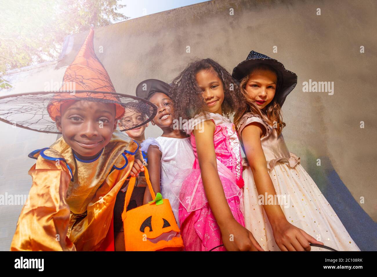 Boy with candy bucket over group of kids in Halloween costumes hug ...