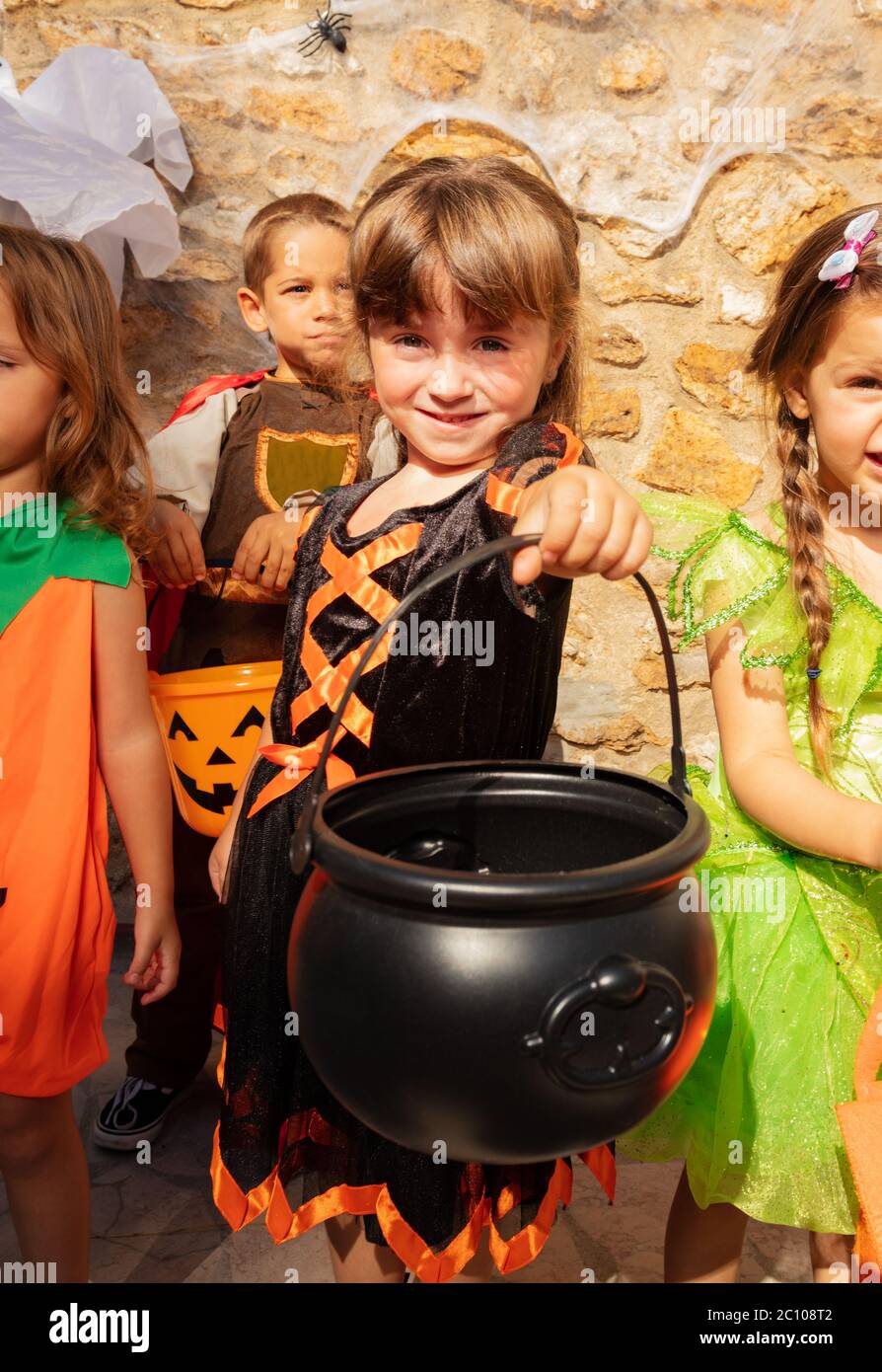 Portrait of a little girl hold bucket for candies standing in a group ...