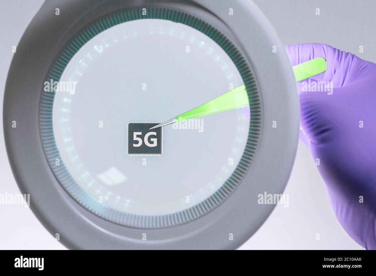 Hand in glove holding 5G microchip with pair of tweezers under ...