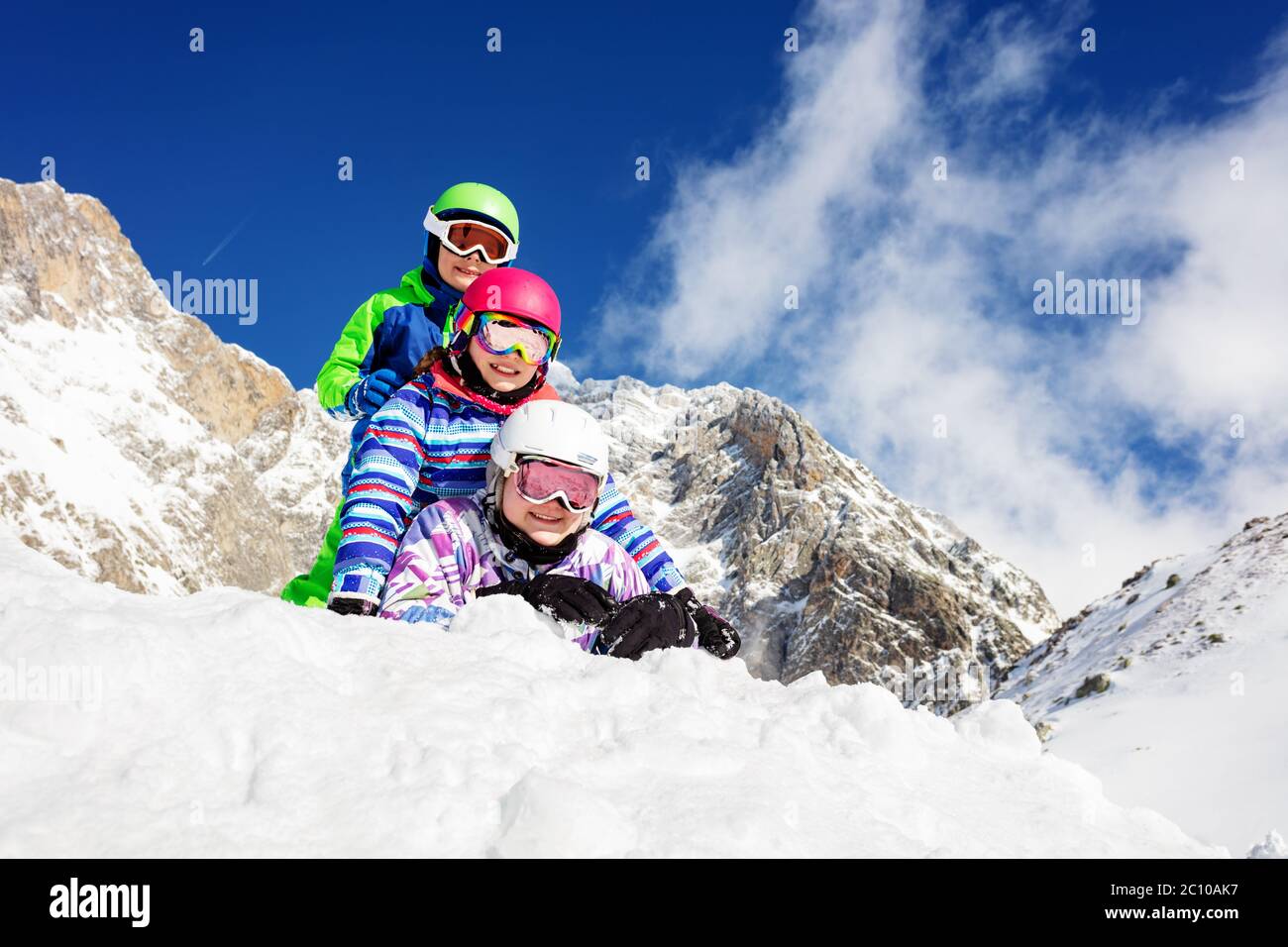 Portrait of three happy children lay on top of each other in the snow ...