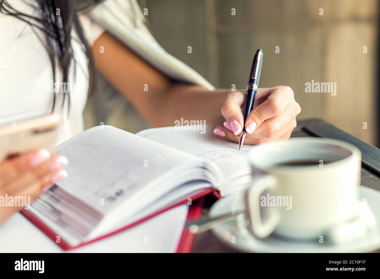 Young woman right hand writing plans on small diary in cafe close up ...
