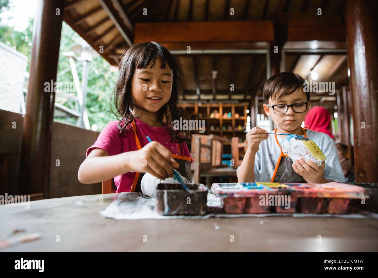Little girl and a boy making handicraft and painting ceramic object at ...