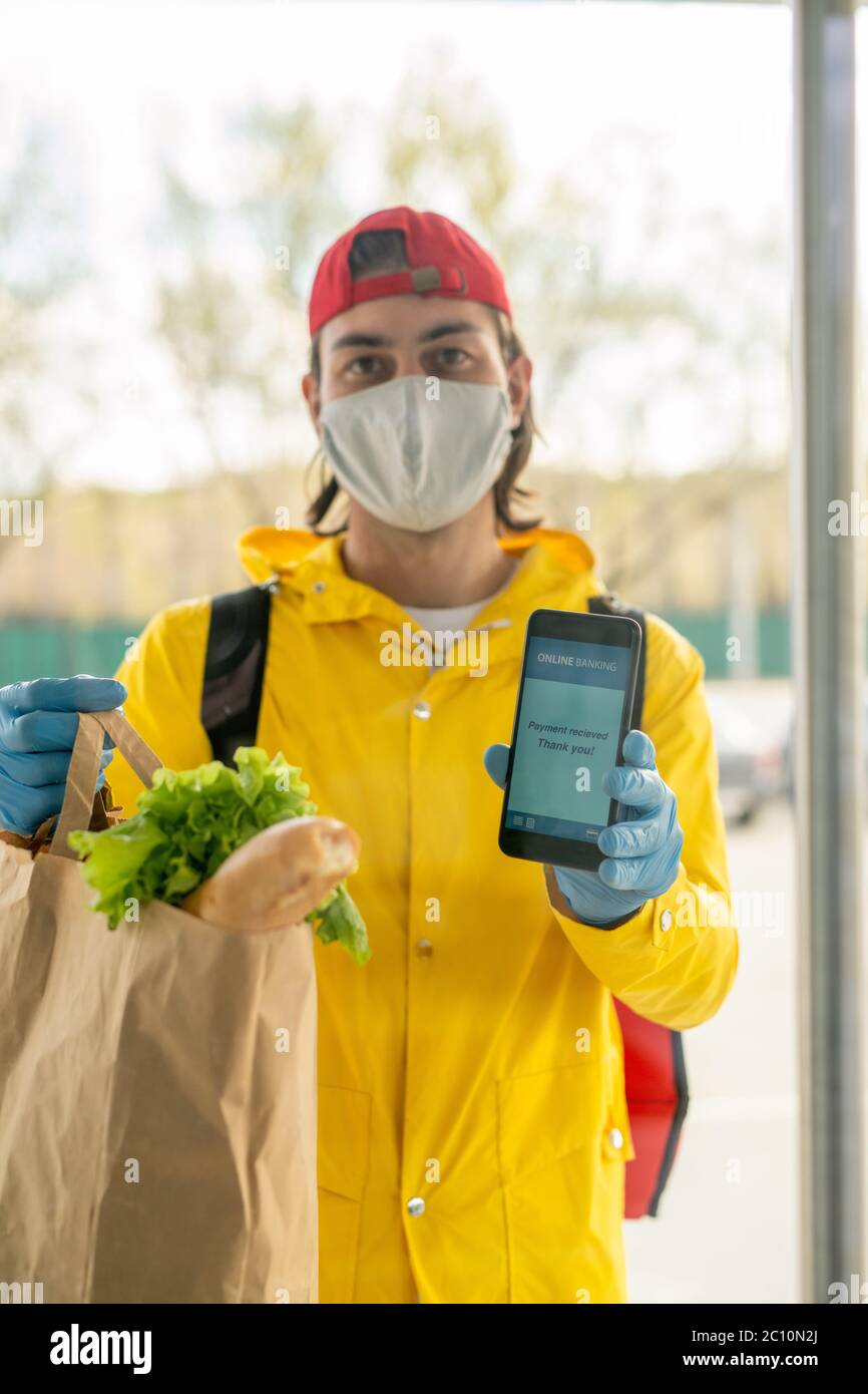 Portrait of delivery man in mask and yellow coat showing message on ...