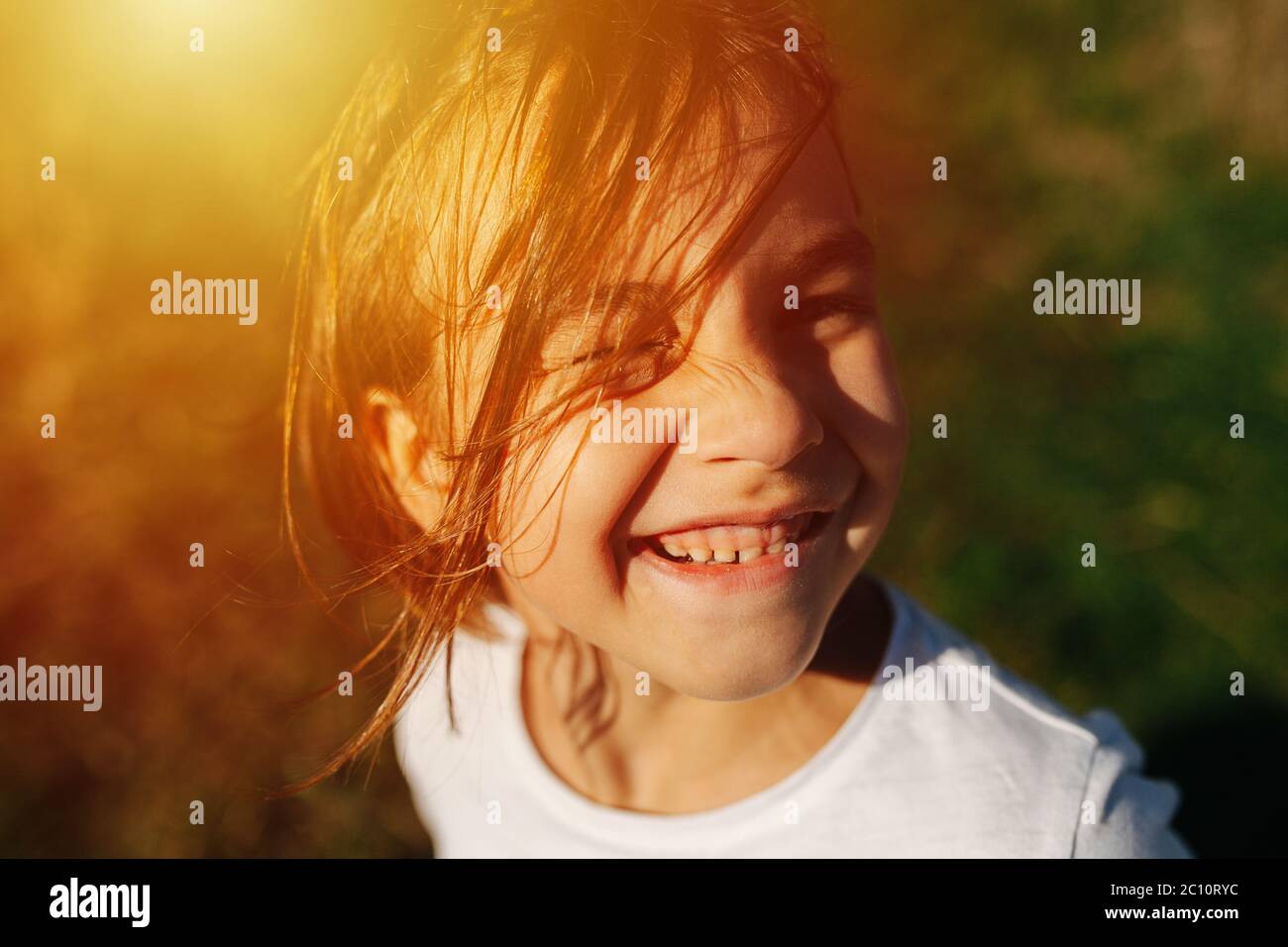 Portrait of a cute little girl, squinting under an orange sunlight ...