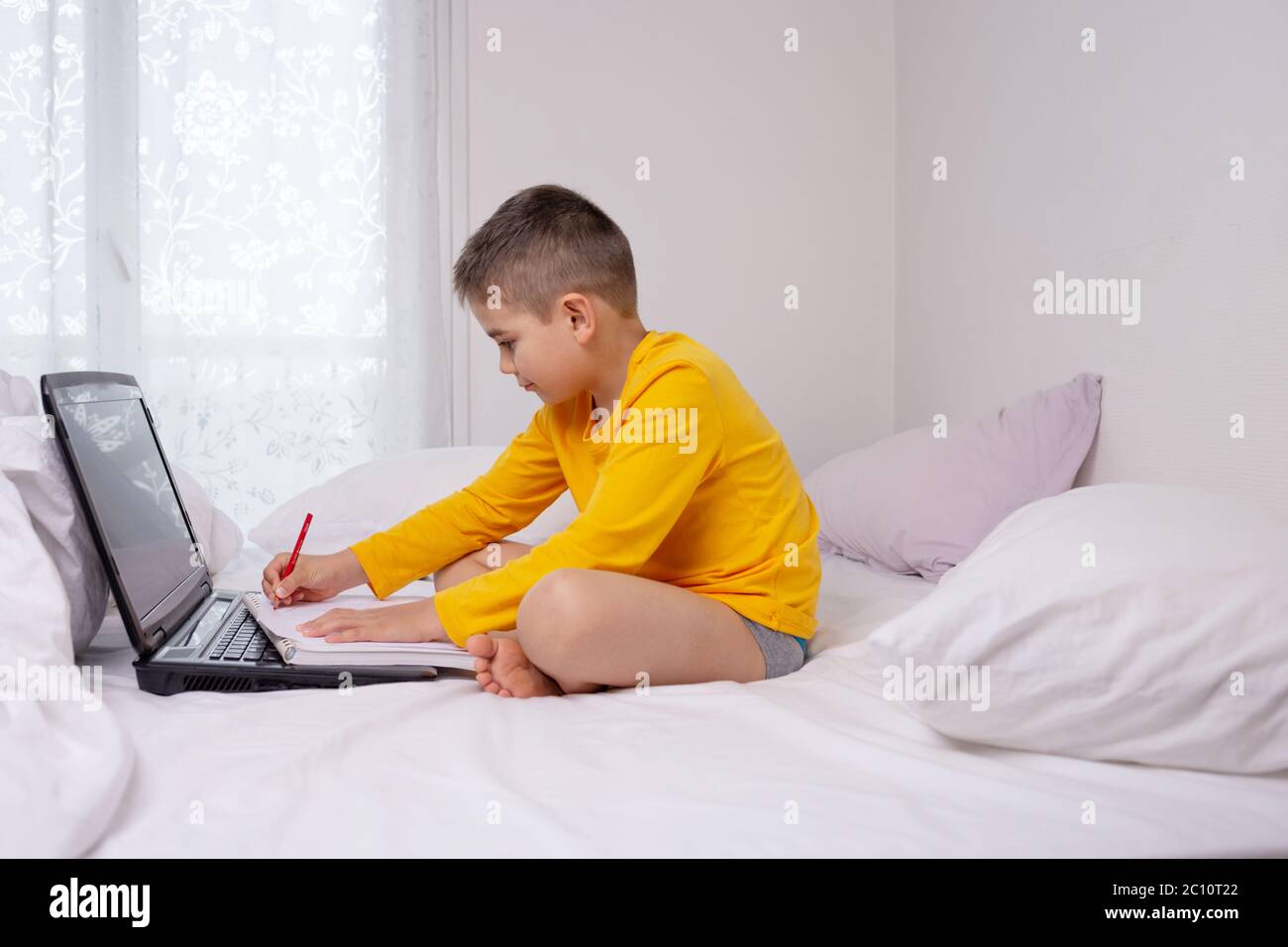 boy doing homework sitting on bed, laptop, handwriting exercise Stock ...