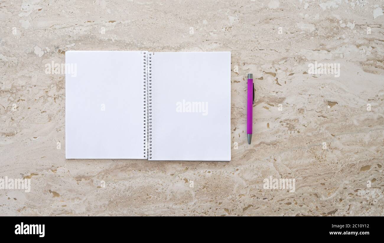 Wide image of blank open notebook and purple pen placed flat on sand ...