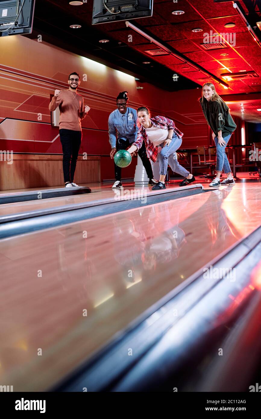 Group of young intercultural cheerful friends playing bowling together ...