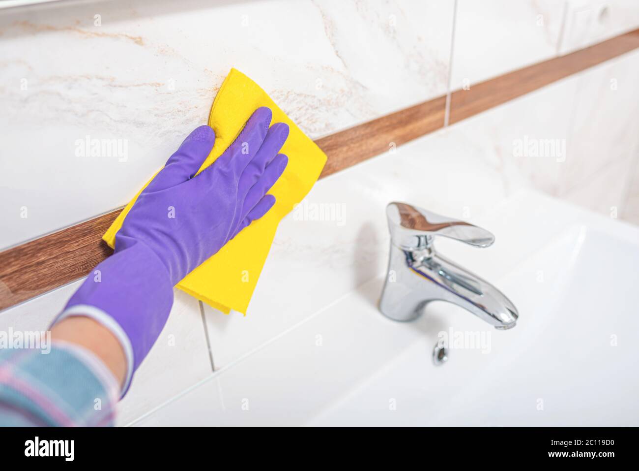 Cleaning in the bathroom. A woman wipes the sink and washbasin faucet ...