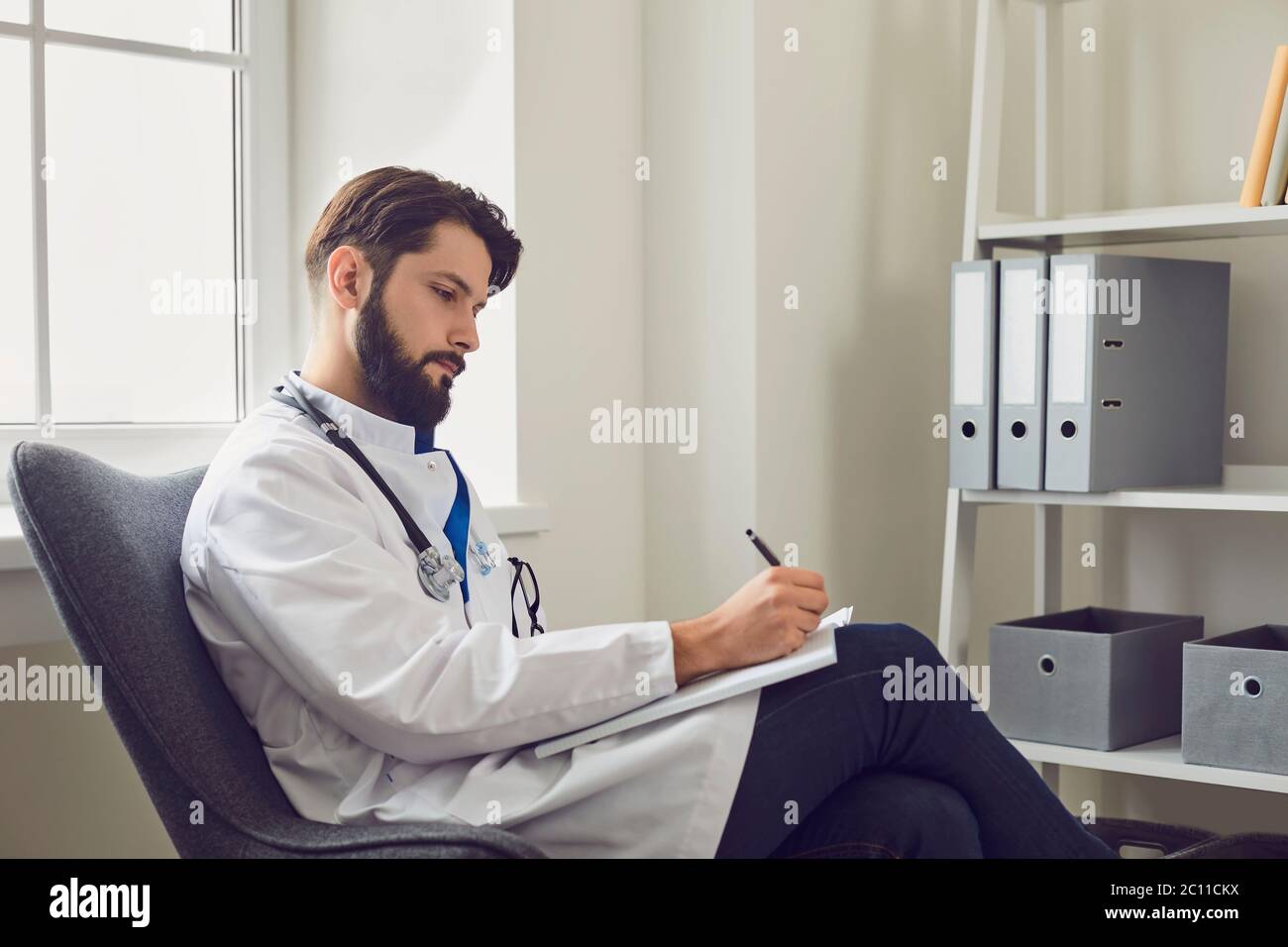 Side view of young male doctor writing case report in comfortable ...